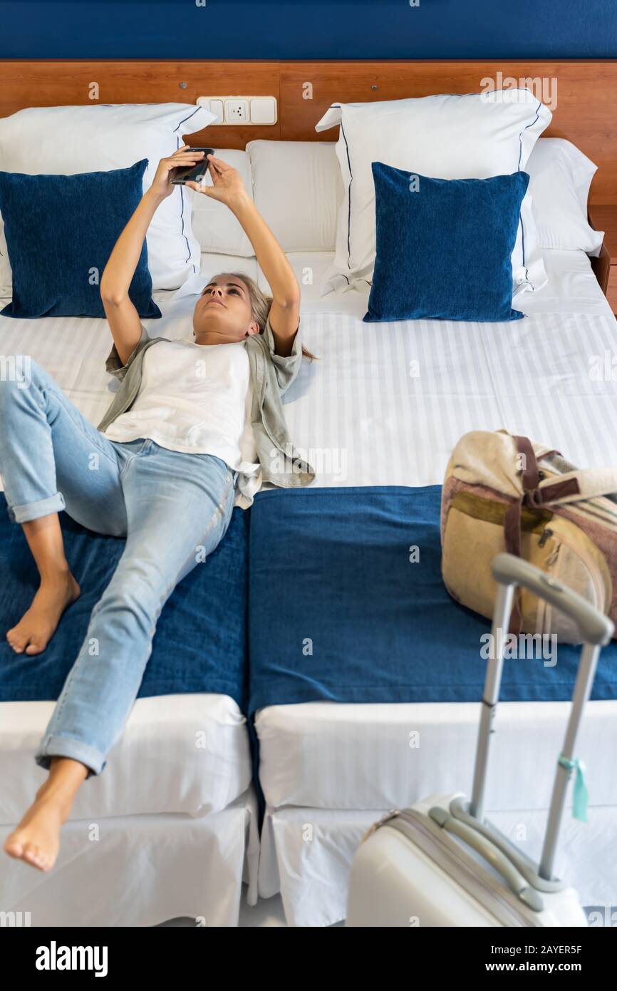 girl looks at the mobile phone stretched out on the hotel bed relaxing ...