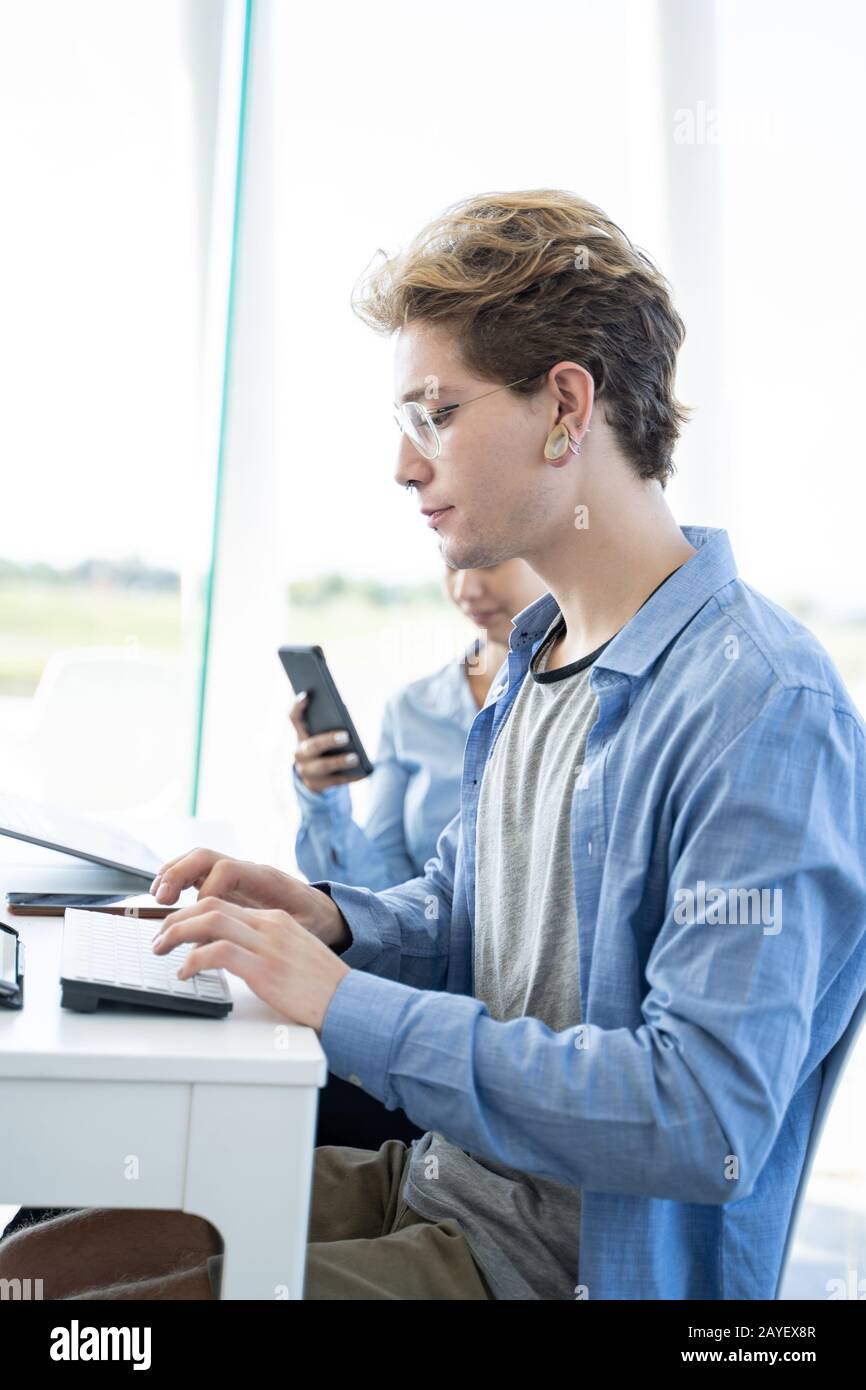 Vertical photo of a young men working on a computer in a coworking with ...