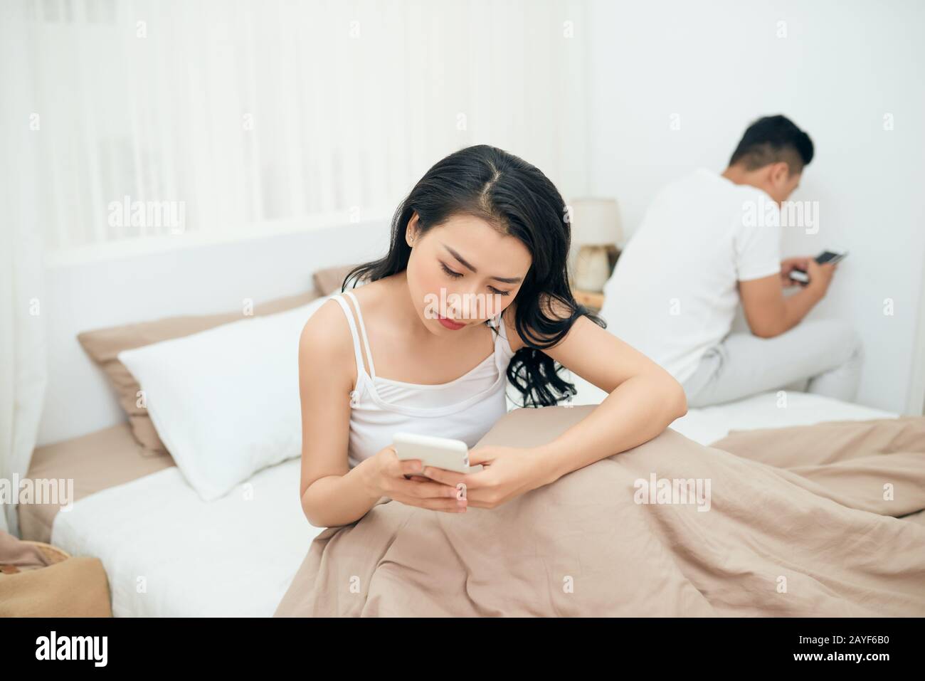 sad view of young married couple using their mobile phone in bed ...