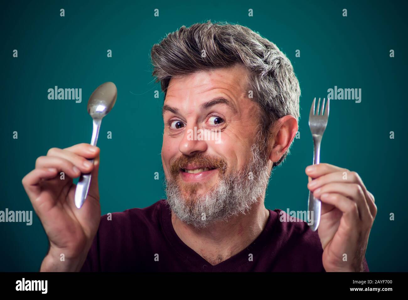 A portrait of bearded hungry man holding spoon and fork in hands ...