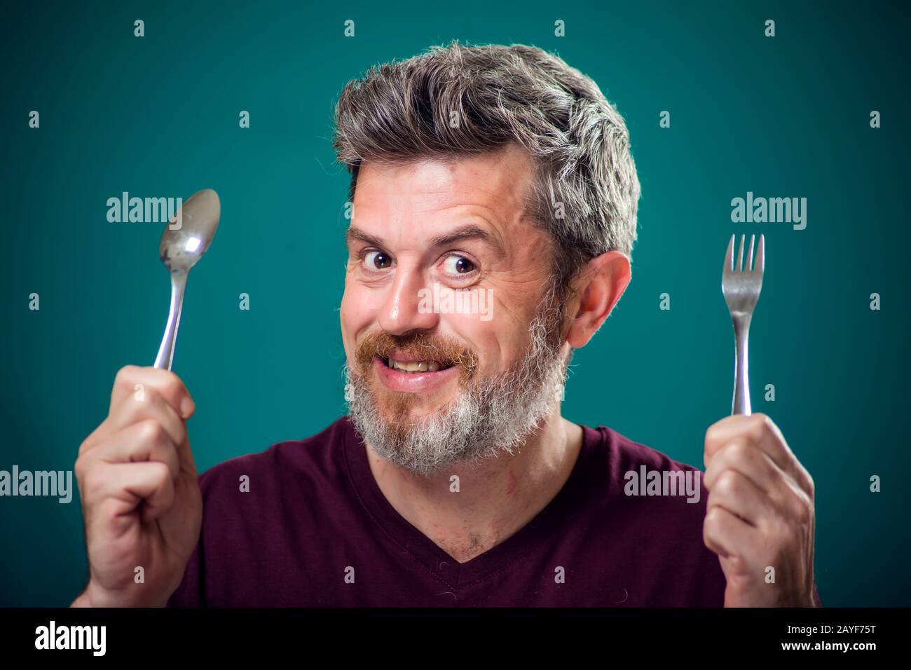 A portrait of bearded hungry man holding spoon and fork in hands ...