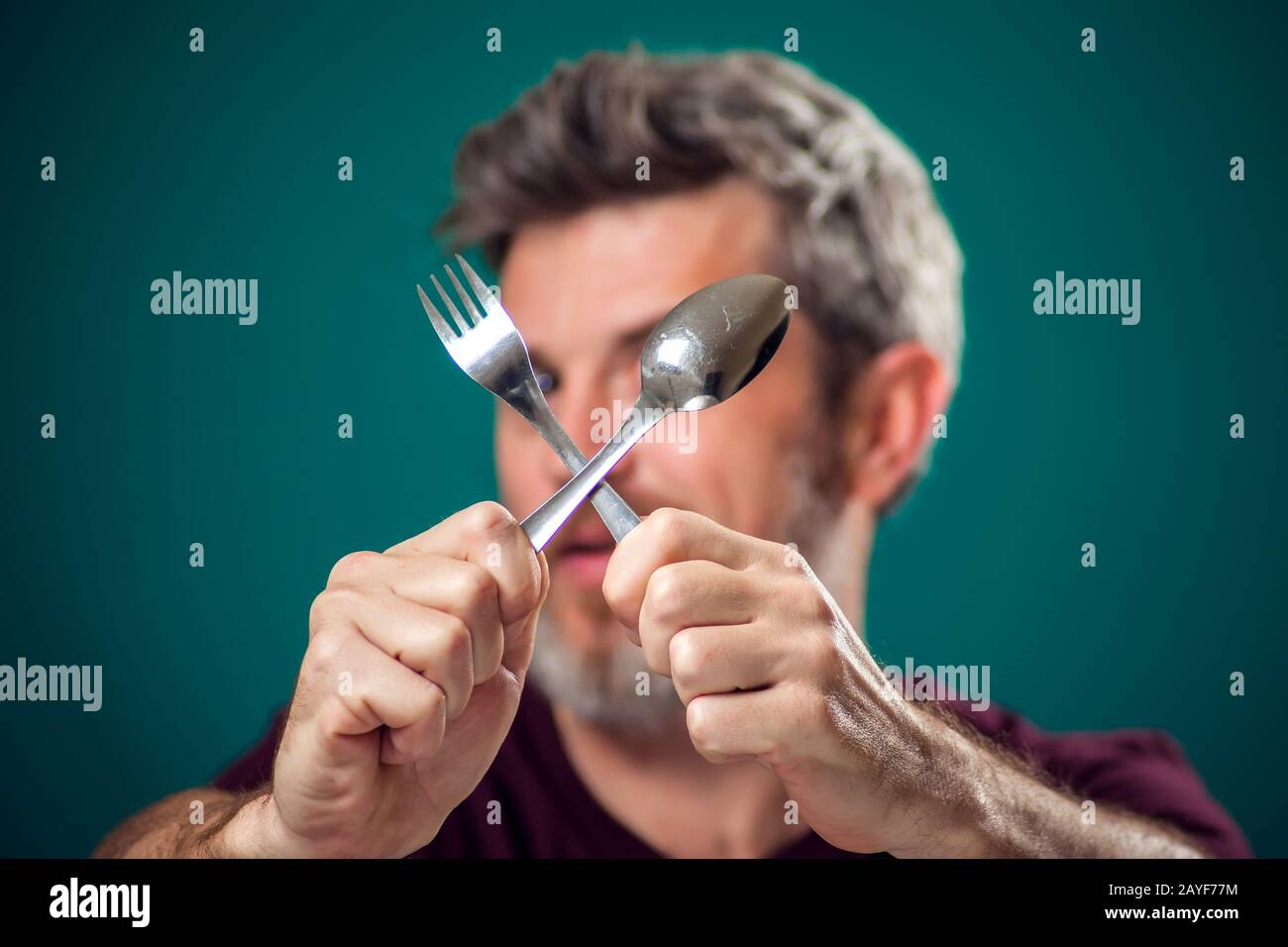 A portrait of bearded hungry man holding spoon and fork in hands ...