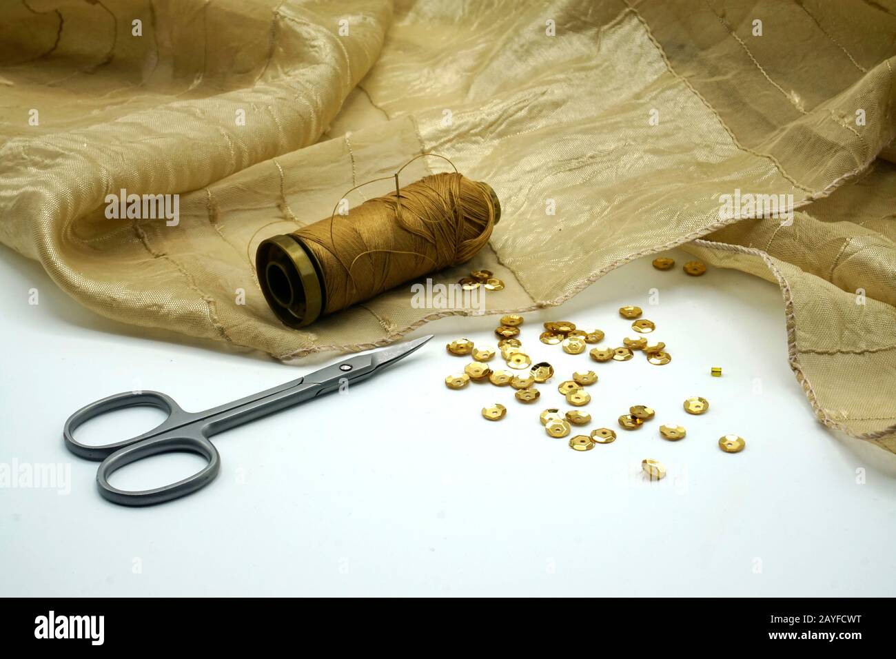 Gold sequins, spool of golden thread, needle on rippled gold silk ...