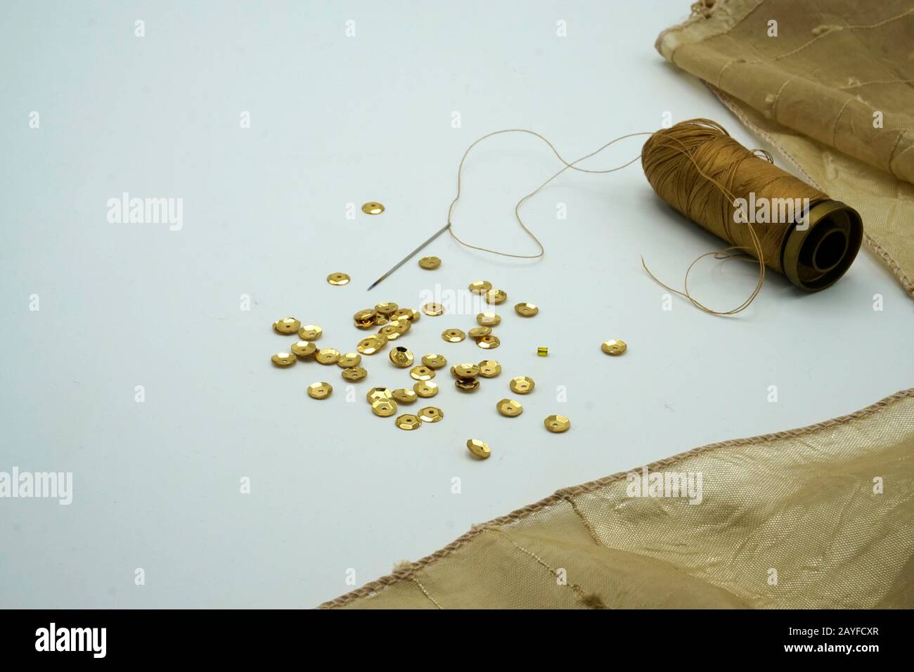 Gold sequins, spool of golden thread, needle on rippled gold silk ...
