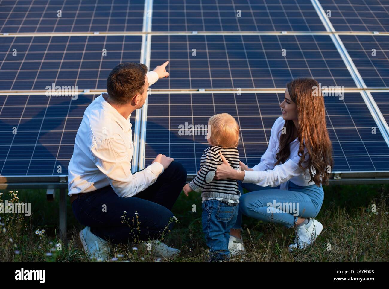 Back view of young family of three crouching near photovoltaic solar ...
