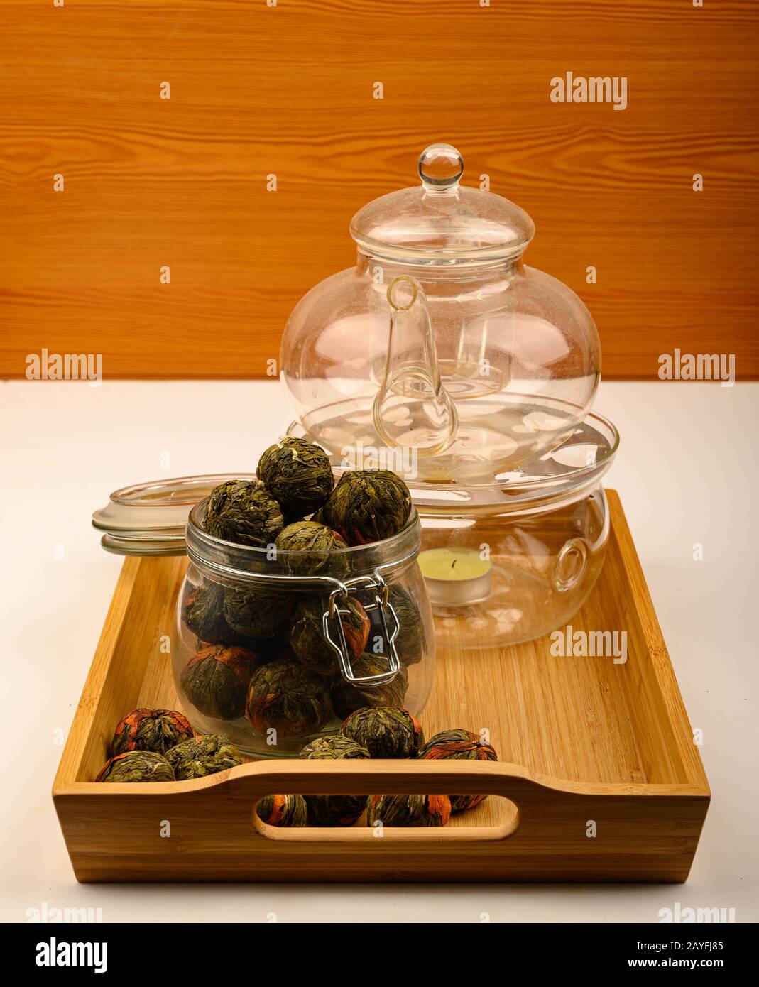 Flower tea balls in a glass jar and a glass teapot on a wooden tray on ...