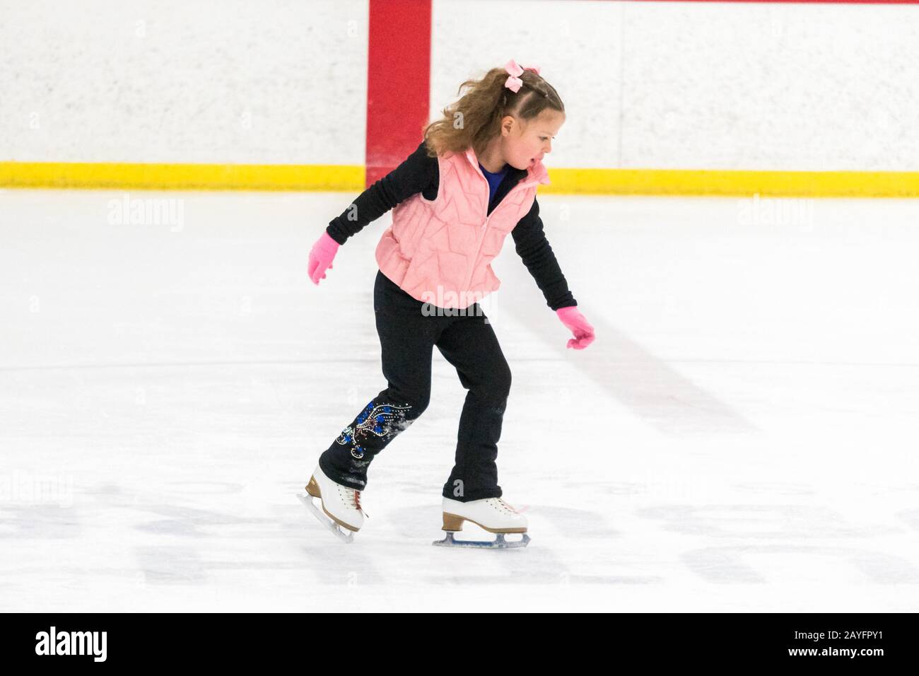 Little girl practicing figure skating moves on the indoor ice rink ...