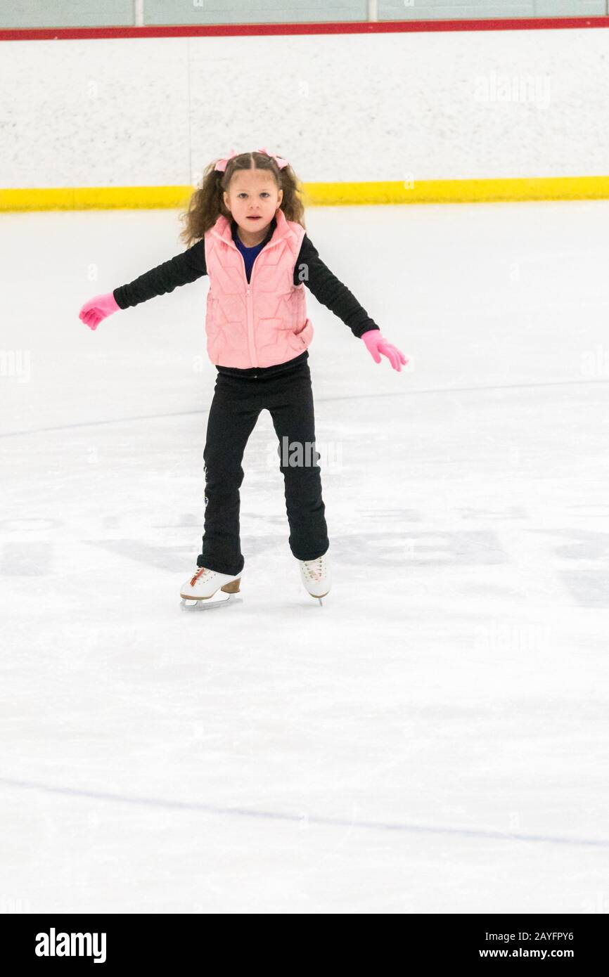 Little girl practicing figure skating moves on the indoor ice rink ...
