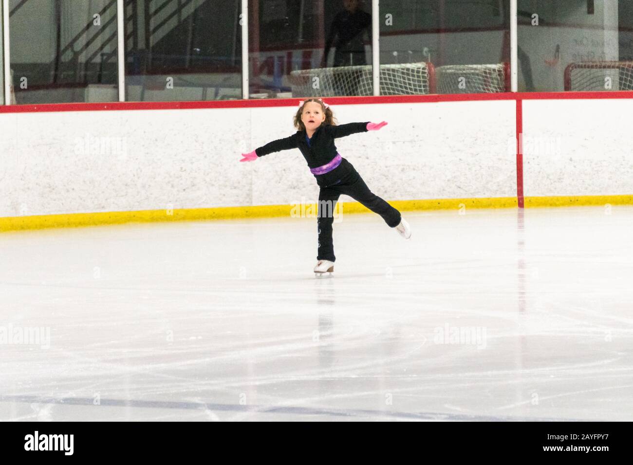 Little girl practicing figure skating moves on the indoor ice rink ...