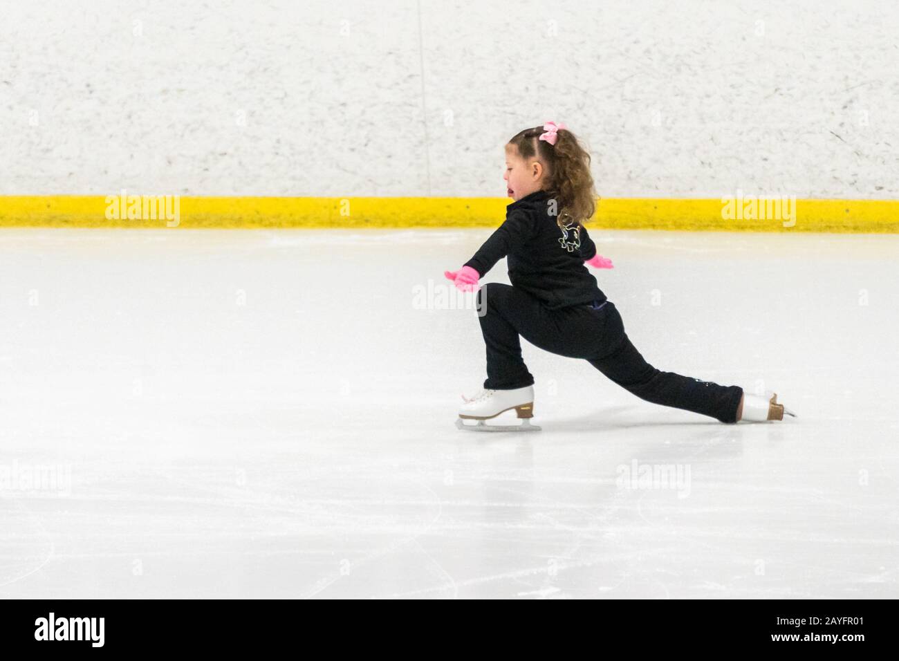 Little girl practicing figure skating moves on the indoor ice rink ...