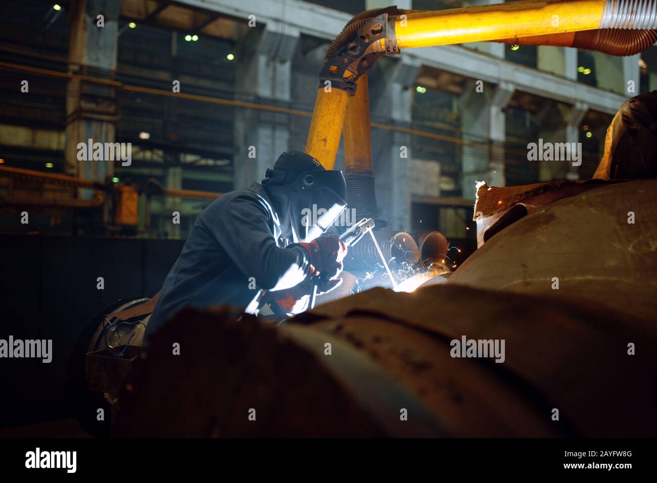 Welder in mask works with metal pipe on factory Stock Photo - Alamy