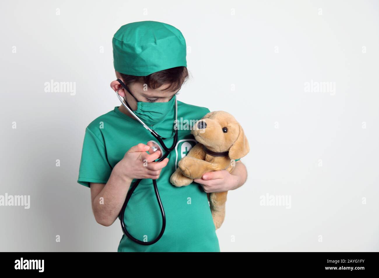 A young child 8yr old boy dressed as a vet holding a toy dog on white ...