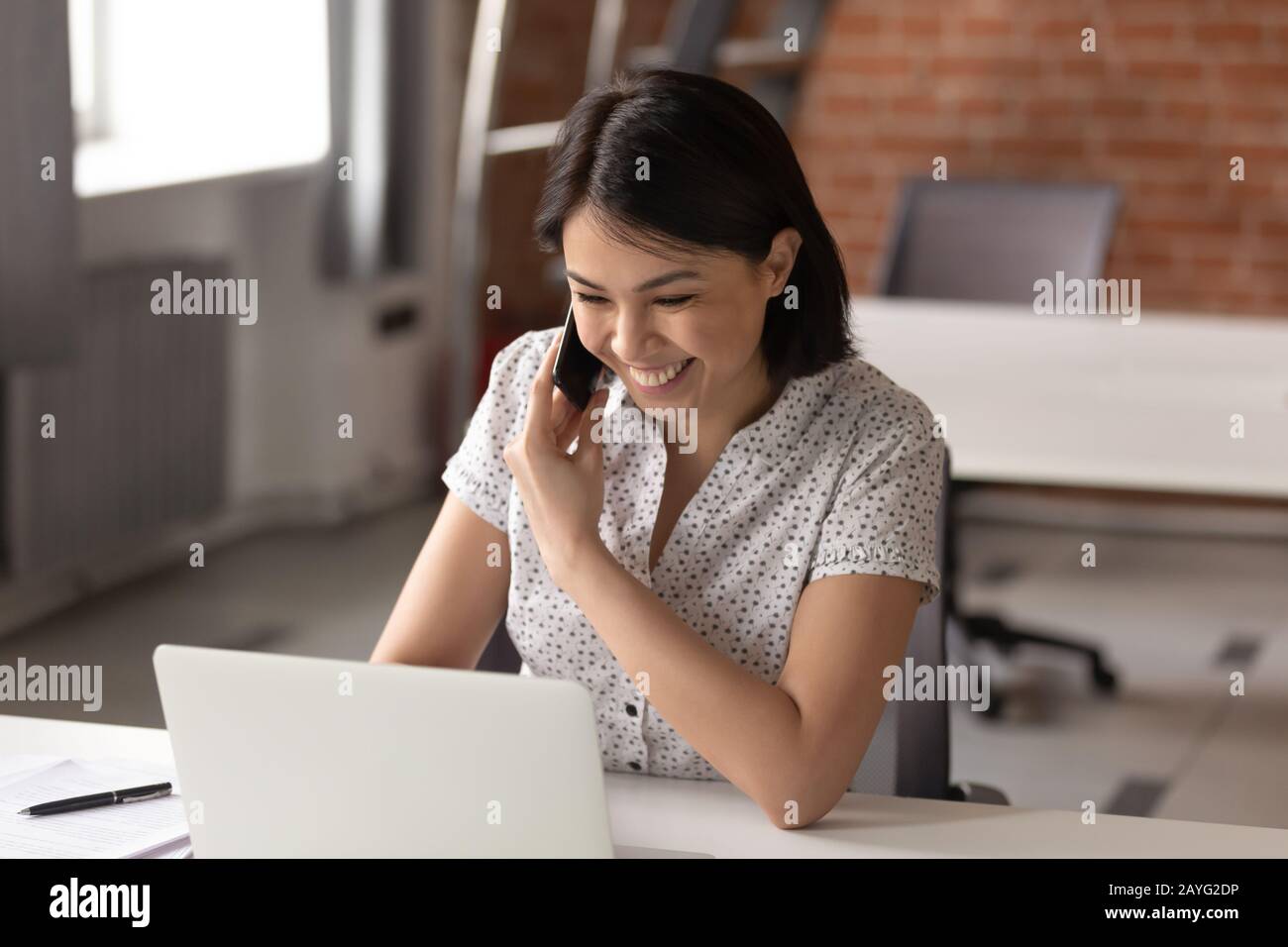Happy female employee speak on cellphone working on laptop Stock Photo ...