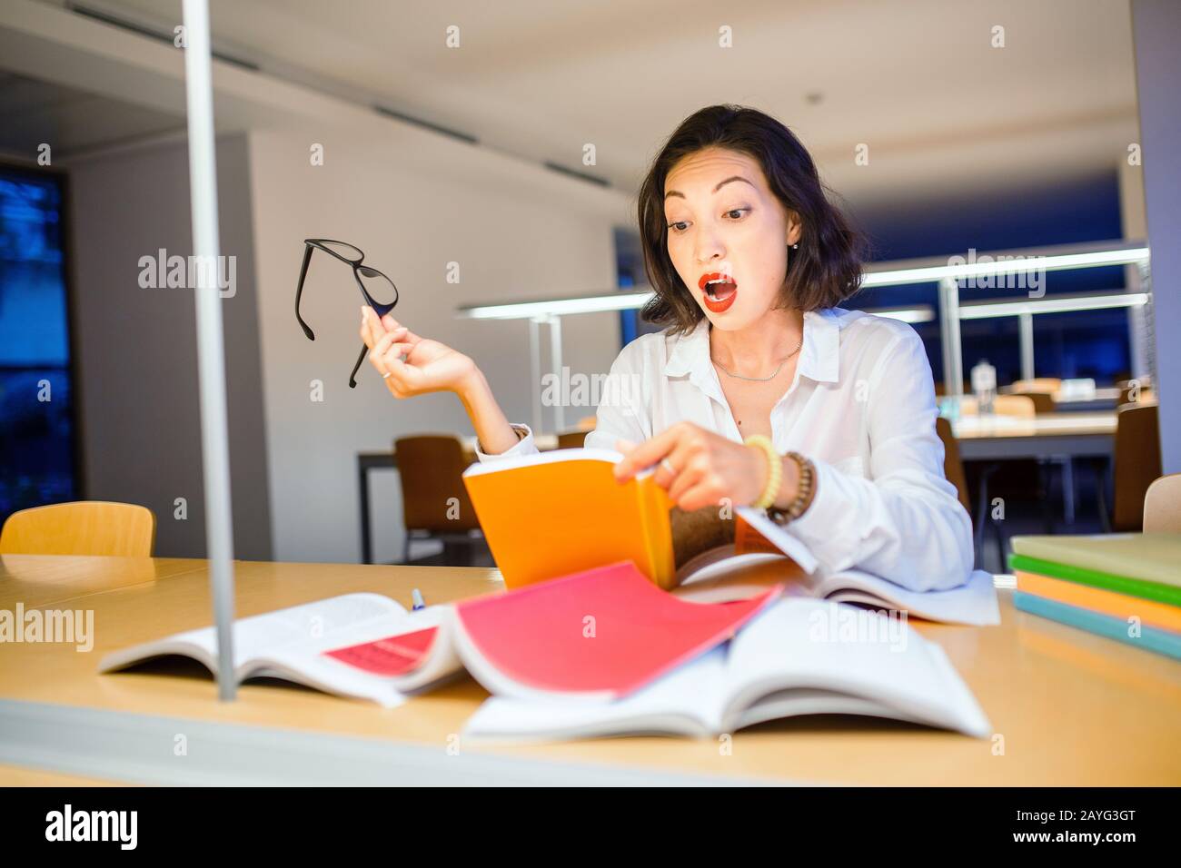 Surprised Woman reading Book in library Stock Photo - Alamy