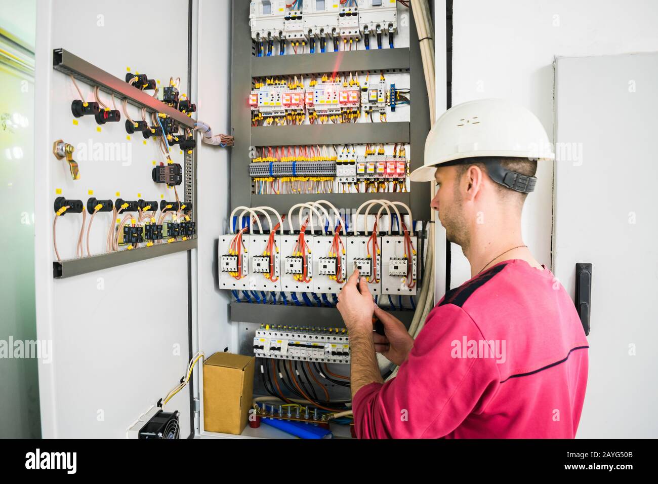 An engineer in a white helmet works in an electrical box. The ...