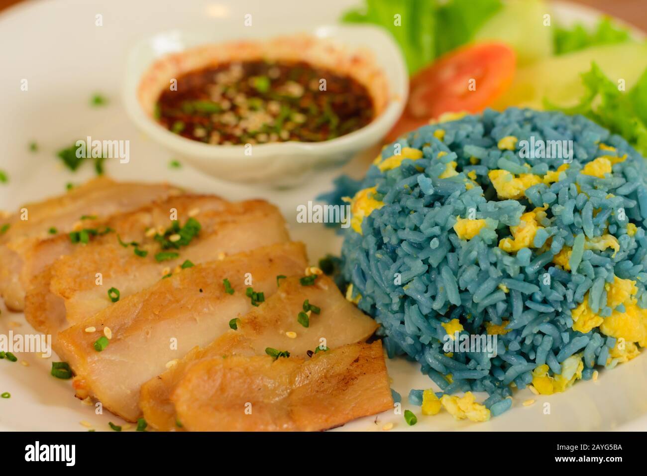 fried blue rice with grilled pork and cucumber slice on a plate. Thai ...