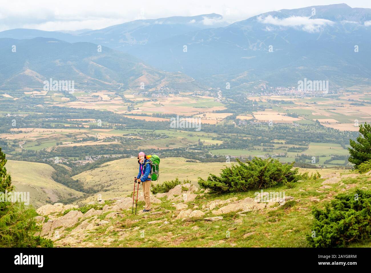 Woman hiker with big backpack stands on the rock and enjoys the valley ...