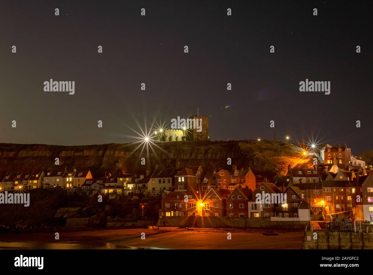 A section of Whitby at night. Houses line the hillside with windows lit ...