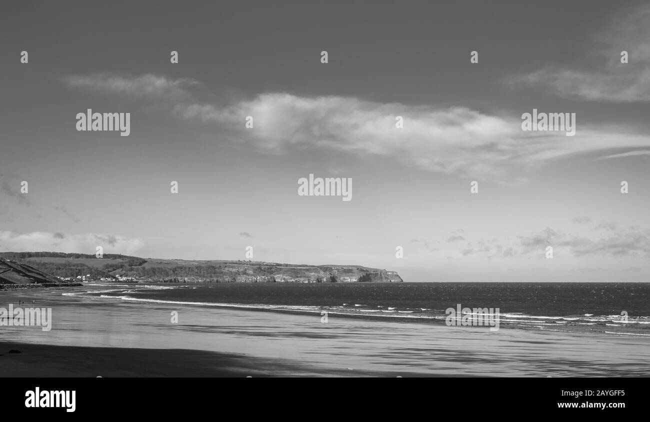 Whitby beach. Waves roll onto a wet beach. In the distance is a ...