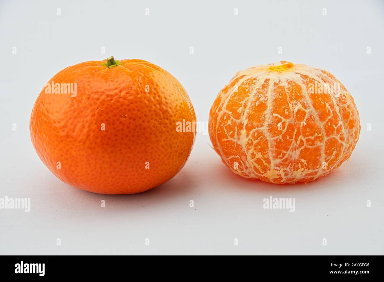 A peeled and unpeeled clementime citrus fruit on a white background ...