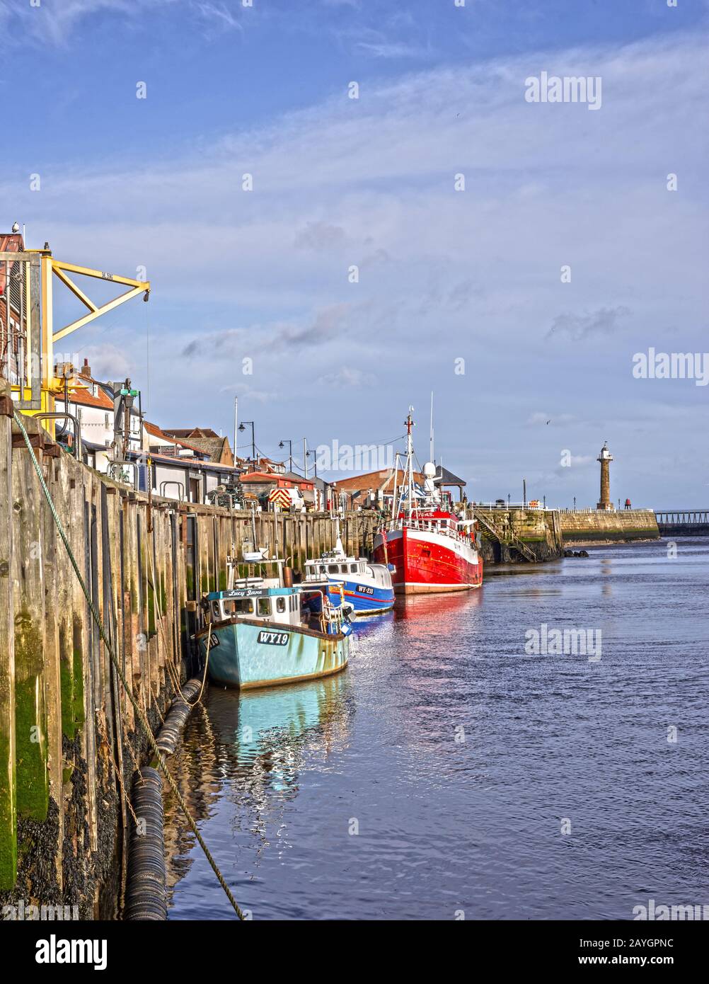 Whitby harbour with three boats moored alongside a wharf. Buildings ...