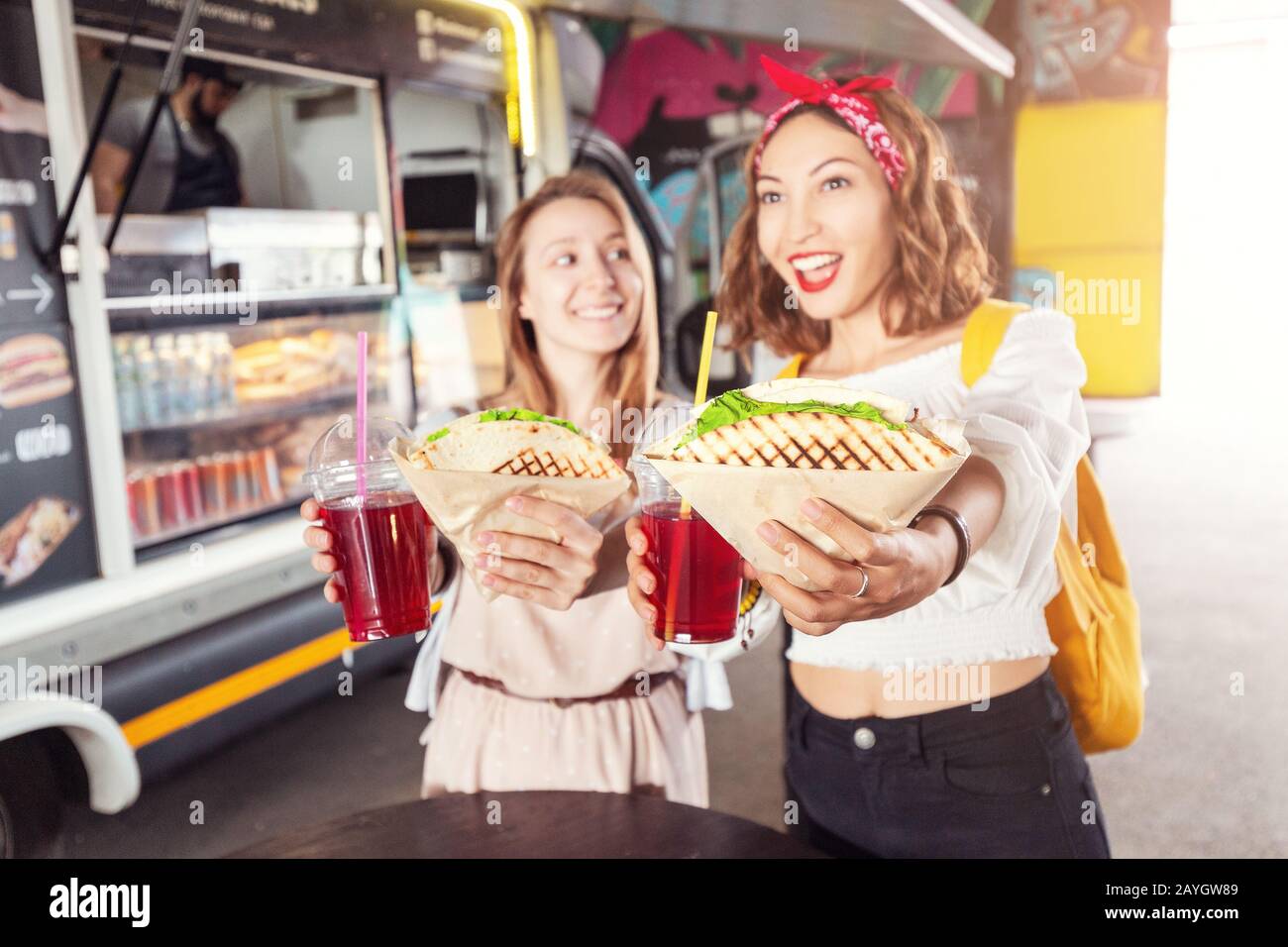 Two happy girls with appetizing fastfood snacks and drinks at the ...