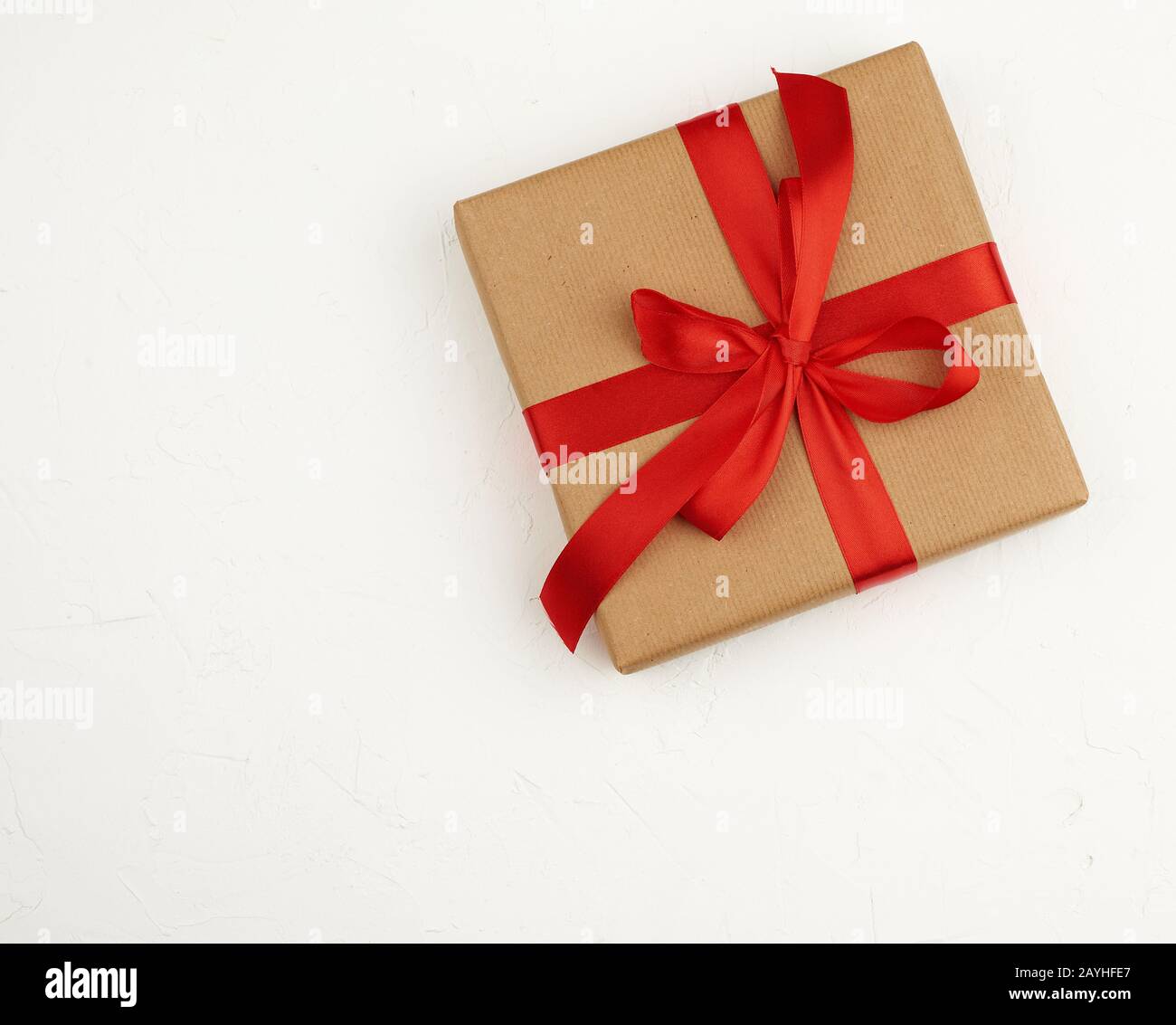 square box wrapped in brown kraft paper and tied with a red silk ribbon ...