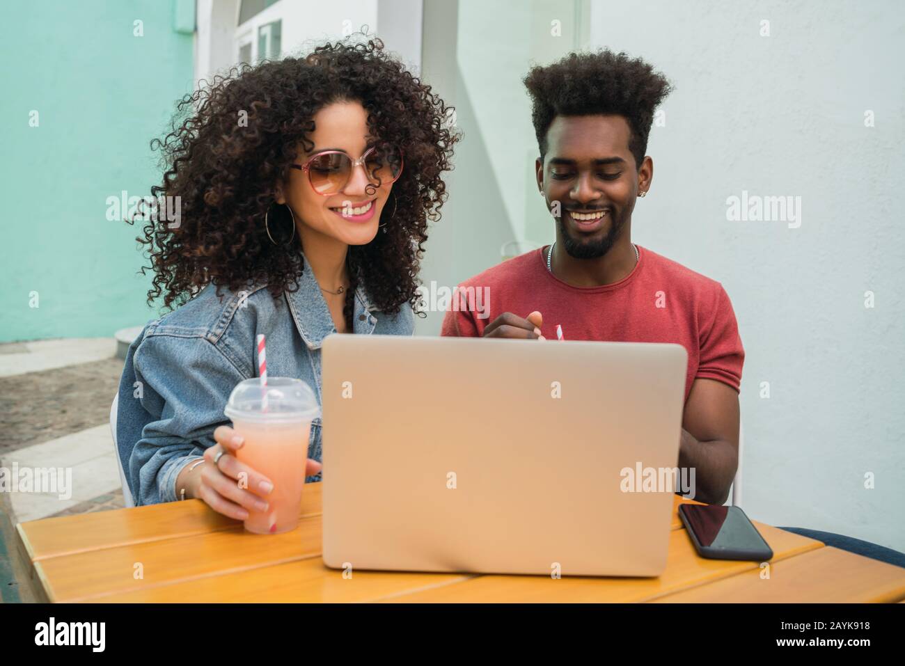 Portrait of two Afro friends using laptop while drinking fresh fruit ...