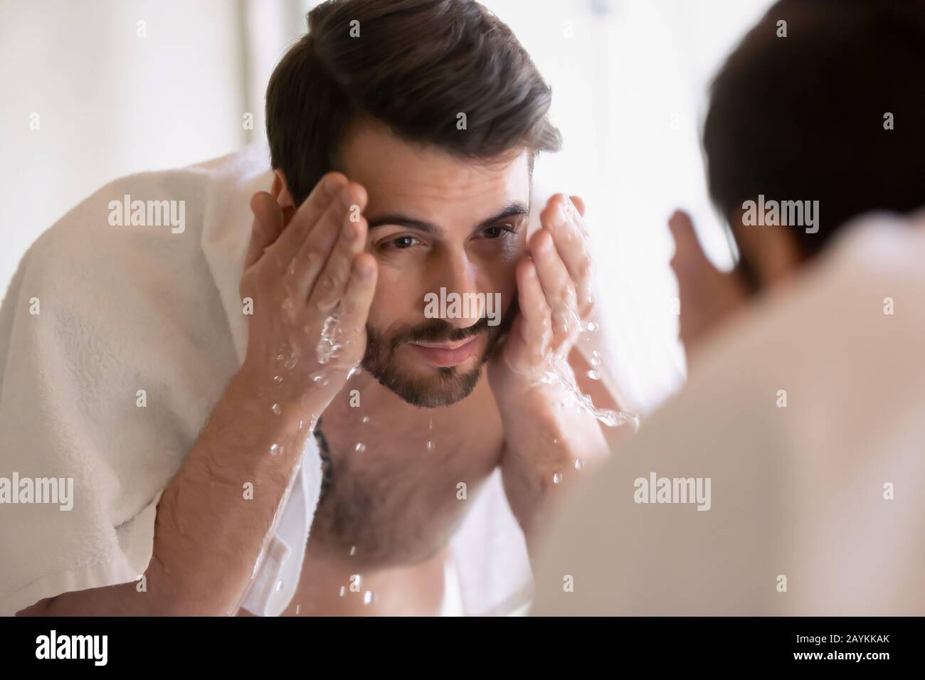 Young man look in mirror washing face in bathroom Stock Photo - Alamy