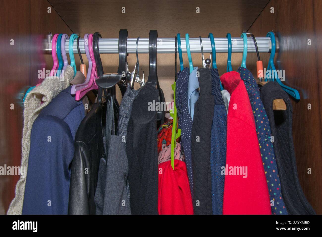 Different clothes are hanging in the closet on multi-colored hangers ...