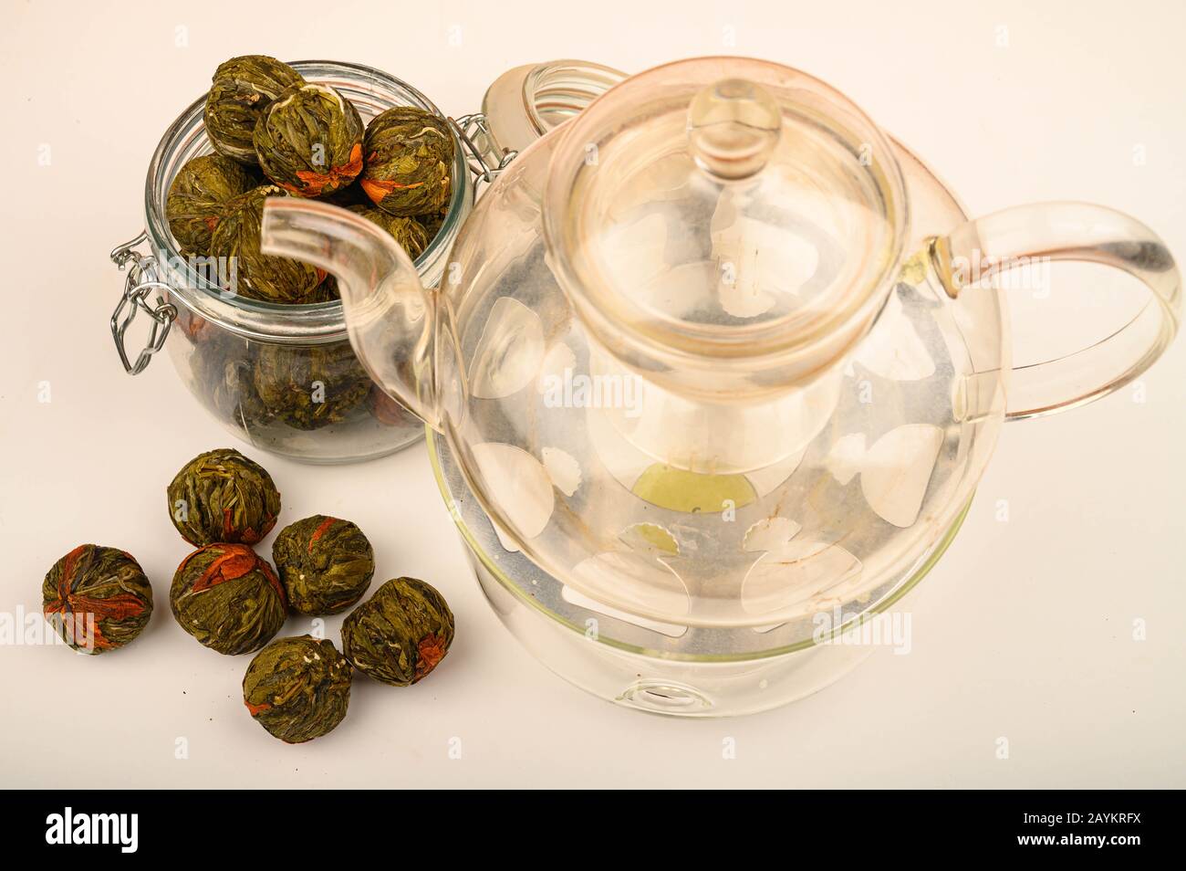 Flower tea balls in a glass jar and a glass teapot on a white ...
