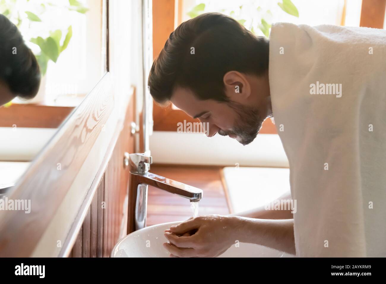 Young man washing face with tap water in bathroom Stock Photo - Alamy