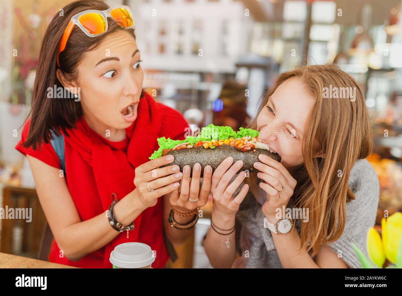 Cheerful multiracial friends eating sandwich and having fun in a cafe ...