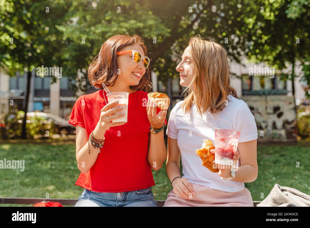 Two young female friends laugh and eat yoghurt outdoors Stock Photo - Alamy