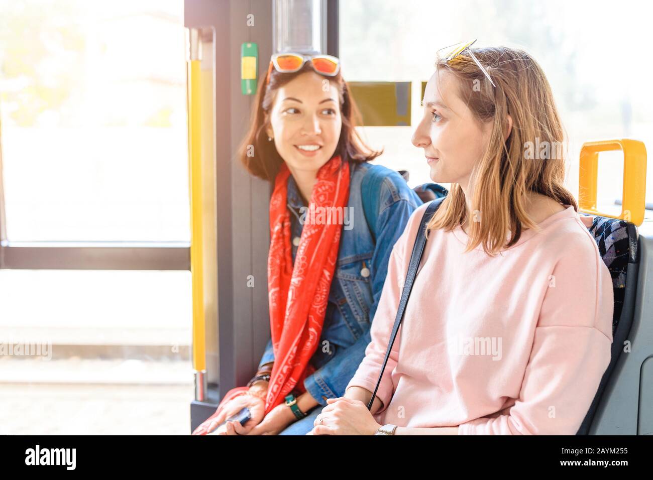 Two cheerful pretty young women are sitting in bus or tram. Public ...