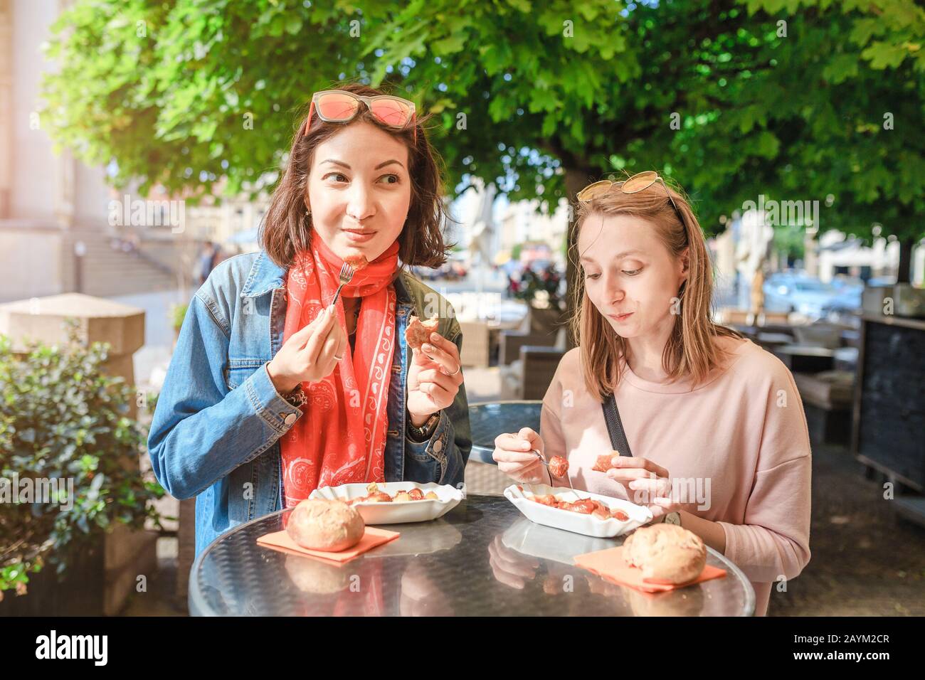 Two girl friends students eating Currywurst fast food German dish pork ...
