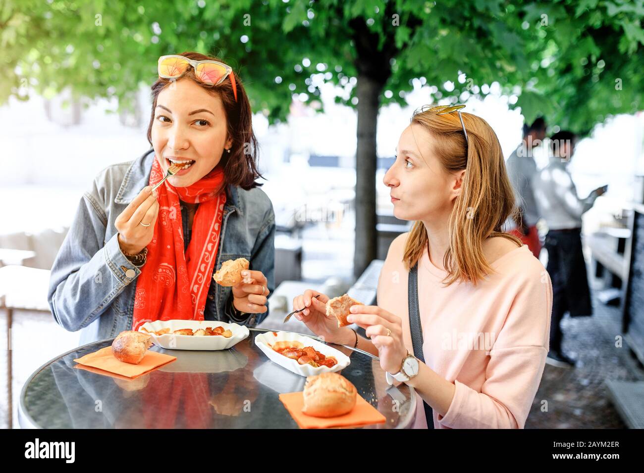 Two girl friends students eating Currywurst fast food German dish pork ...