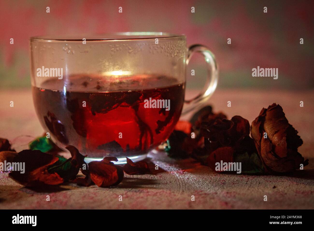 Red Hot Hibiscus tea in a glass mug on a wooden table among rose petals ...