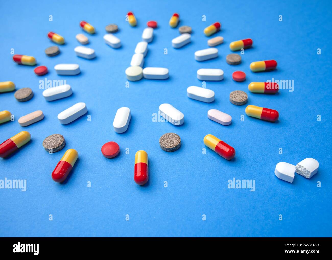 Different types of pills arranged in shape of clock on blue background ...