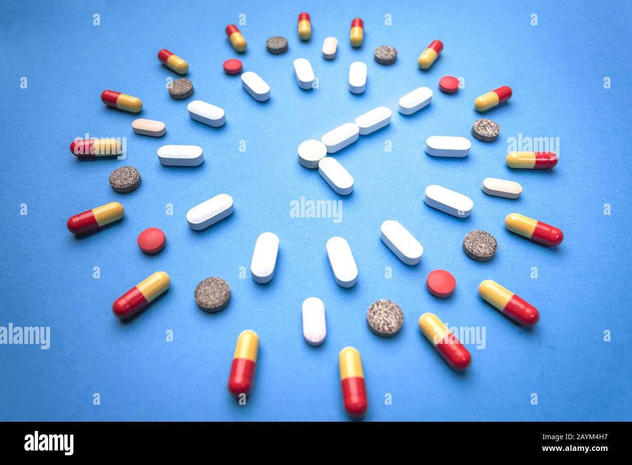 Different types of pills arranged in shape of clock on blue background ...