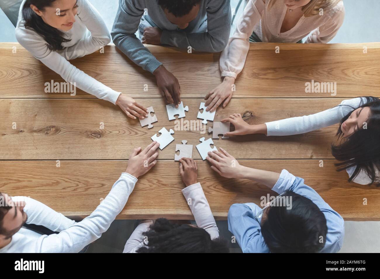 Multiracial team sitting around table, putting together puzzle pieces Stock Photo - Alamy