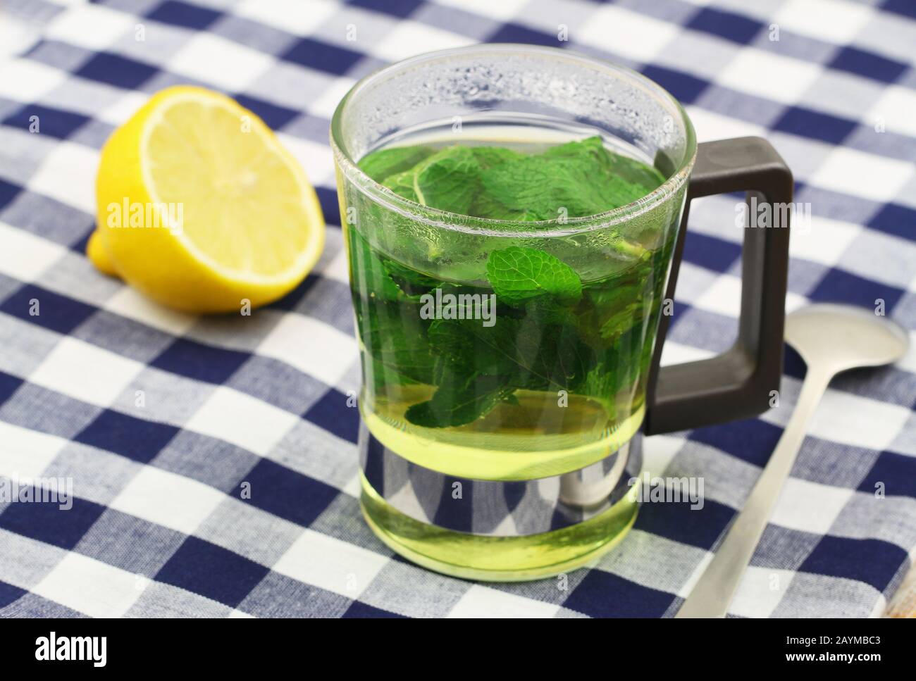 Fresh mint tea in transparent glass and half a lemon on checkered cloth ...