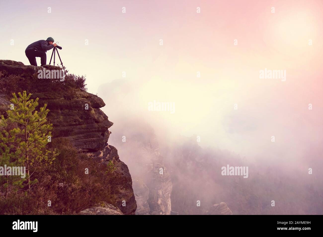 Photographer on mountain cliff looking into mist through viewfinder ...