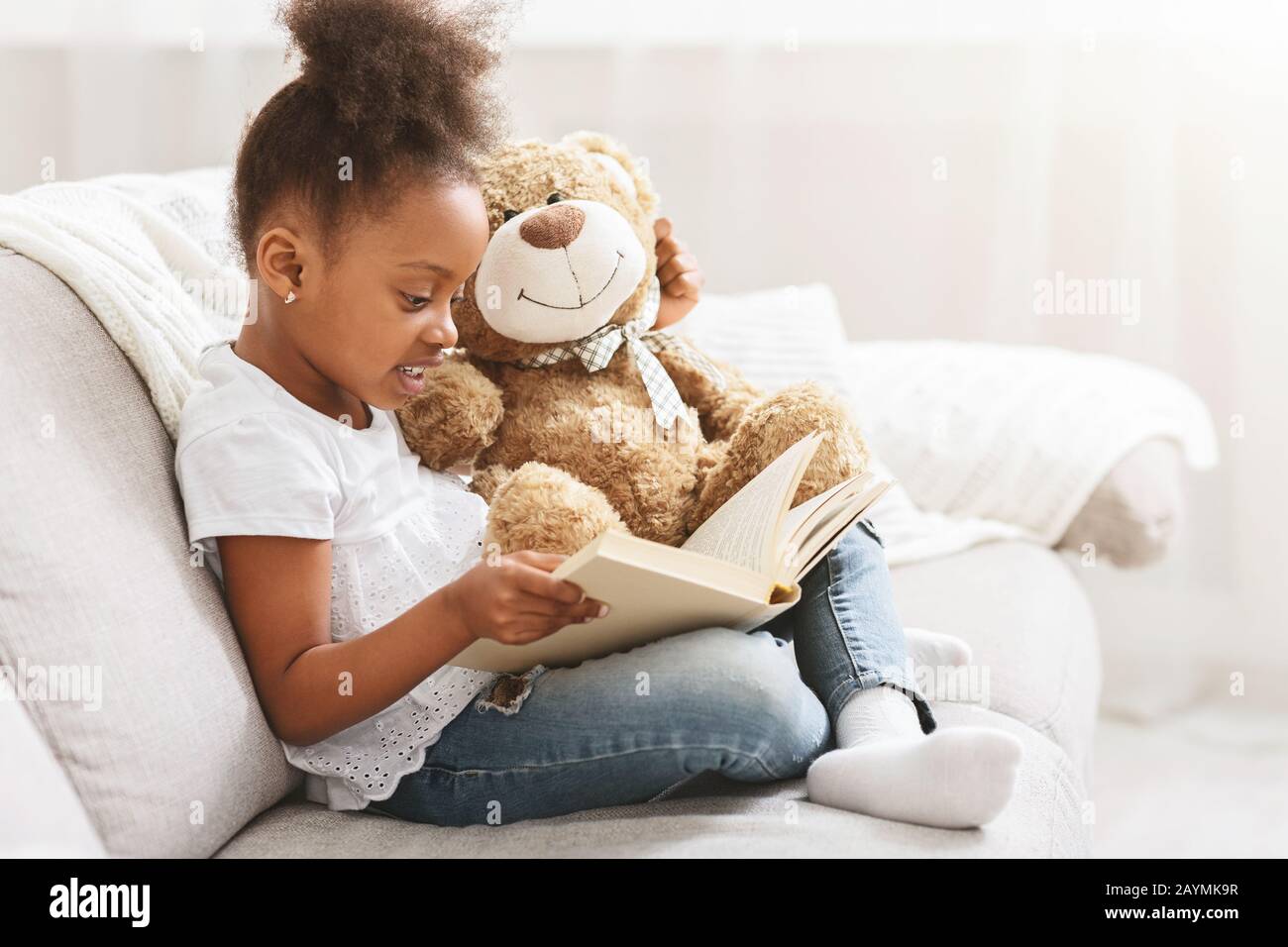 Little afro girl holding teddy bear and reading book Stock Photo - Alamy