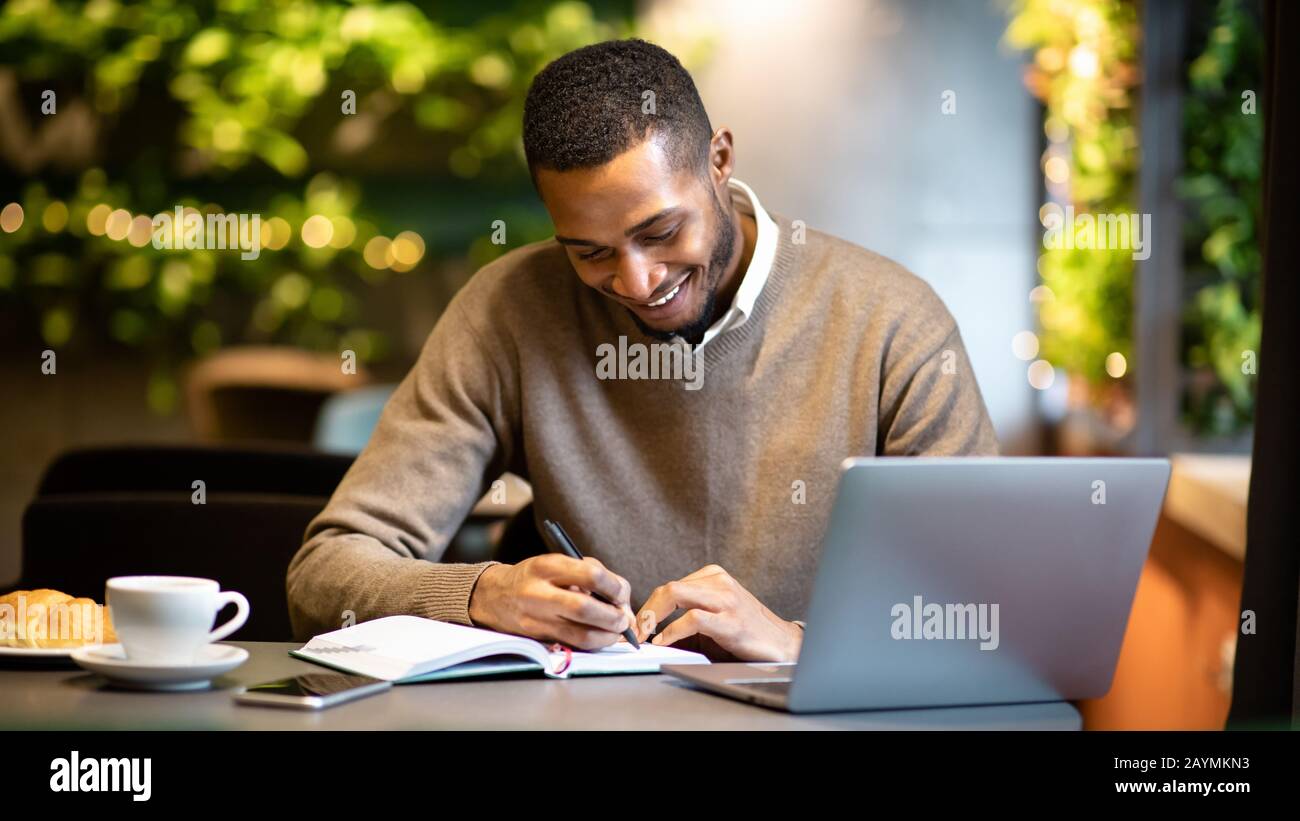 Black man writing in notebook sitting at cafe Stock Photo - Alamy