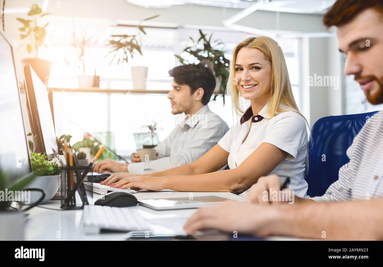 Cheerful blonde girl working in office, sitting next to colleagues Stock Photo - Alamy