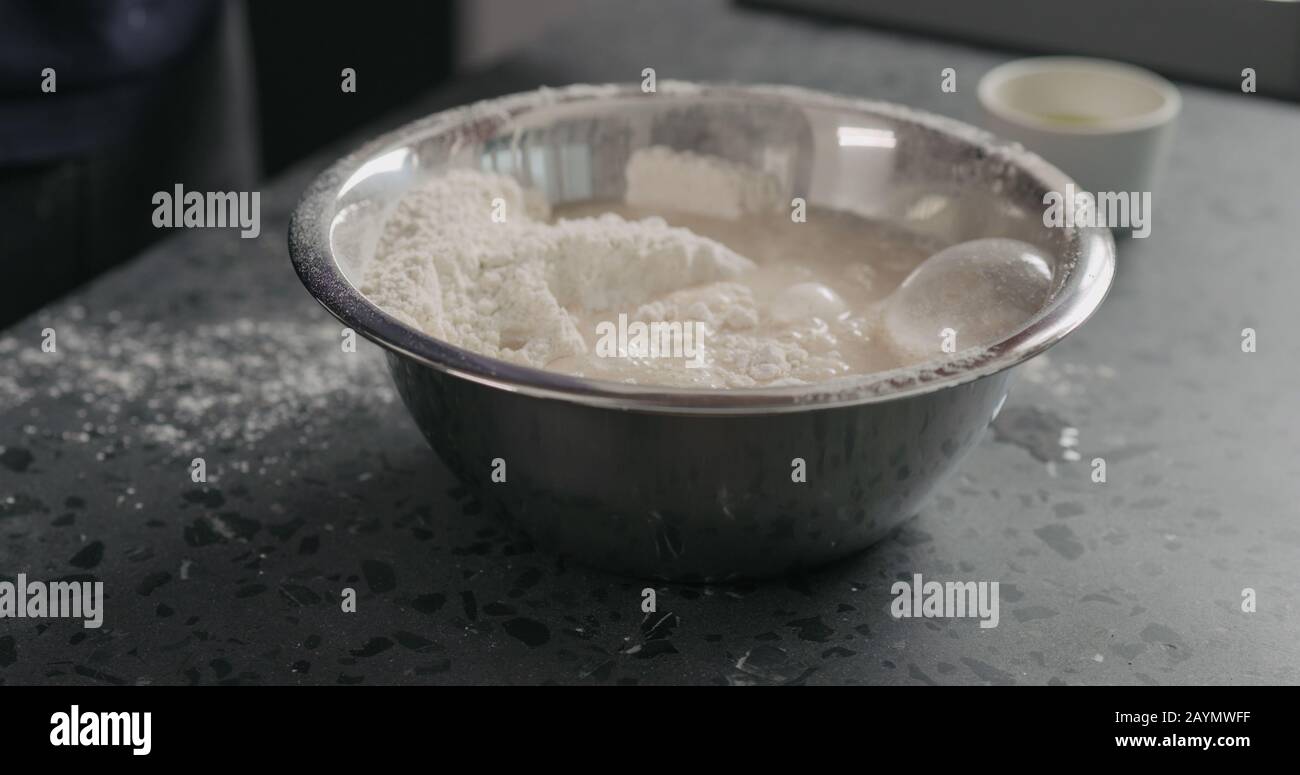 wet ingredients into flour in steel bowl on concrete countertop, wide ...