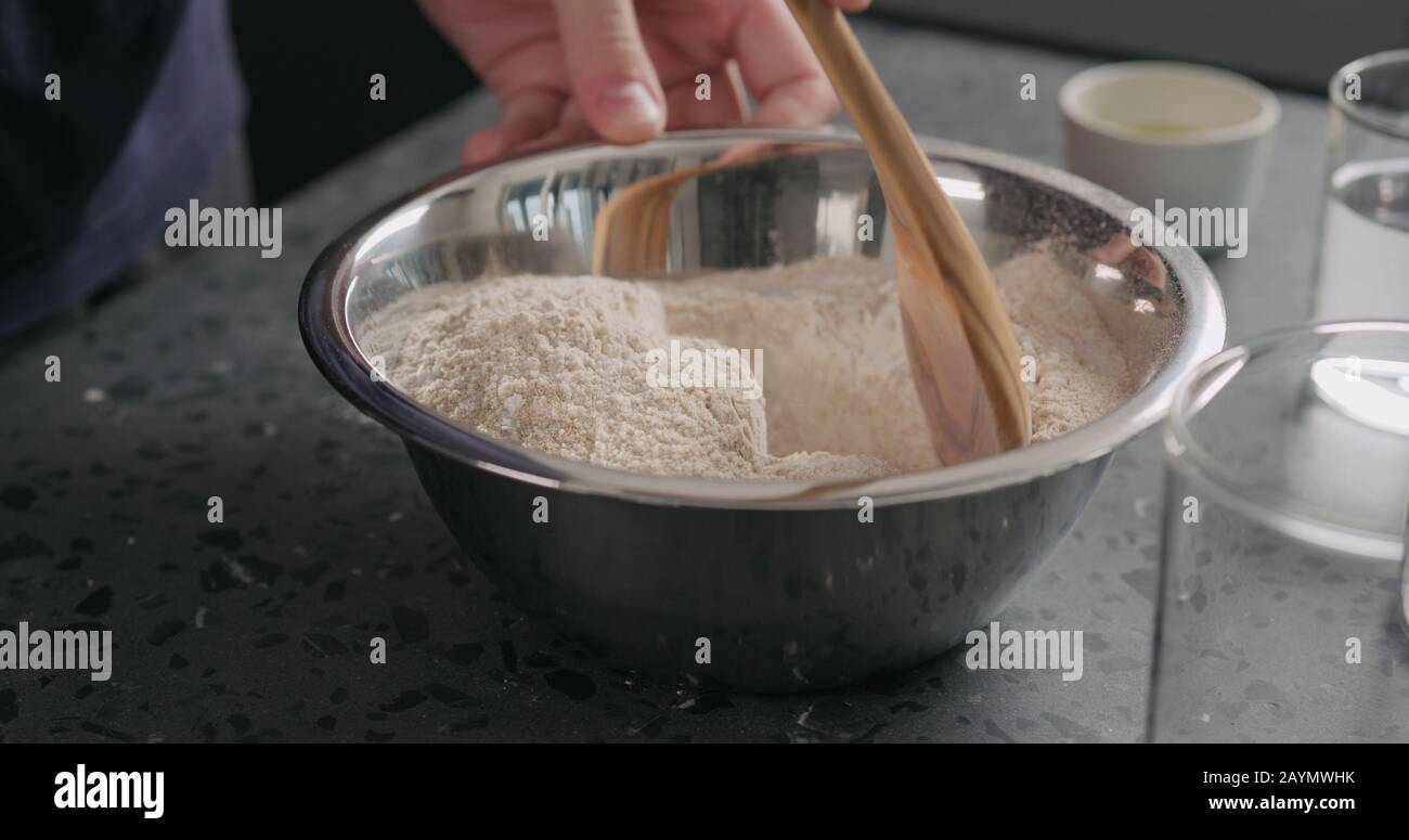 man mixing dry ingredients with flour in steel bowl on concrete ...
