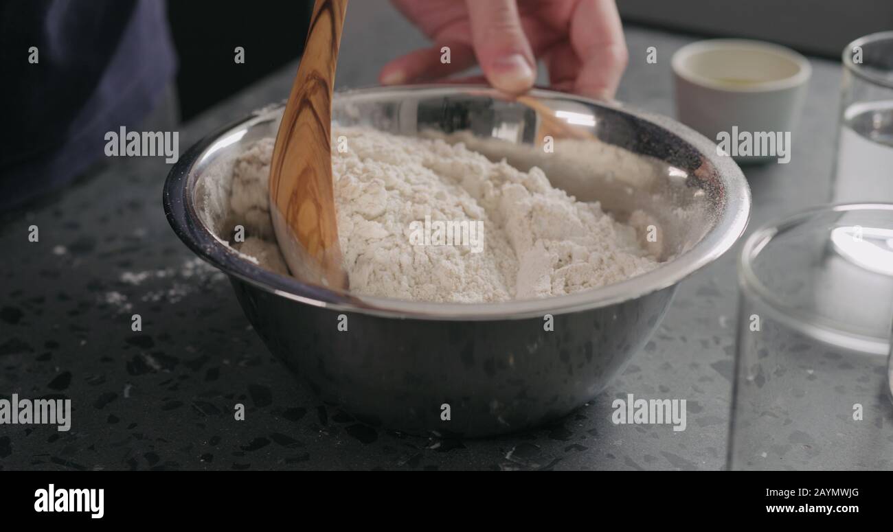 man mixing dry ingredients with flour in steel bowl on concrete ...