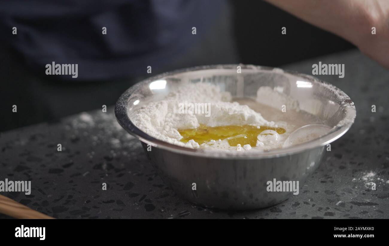 man adds wet ingredients into flour in steel bowl on concrete ...